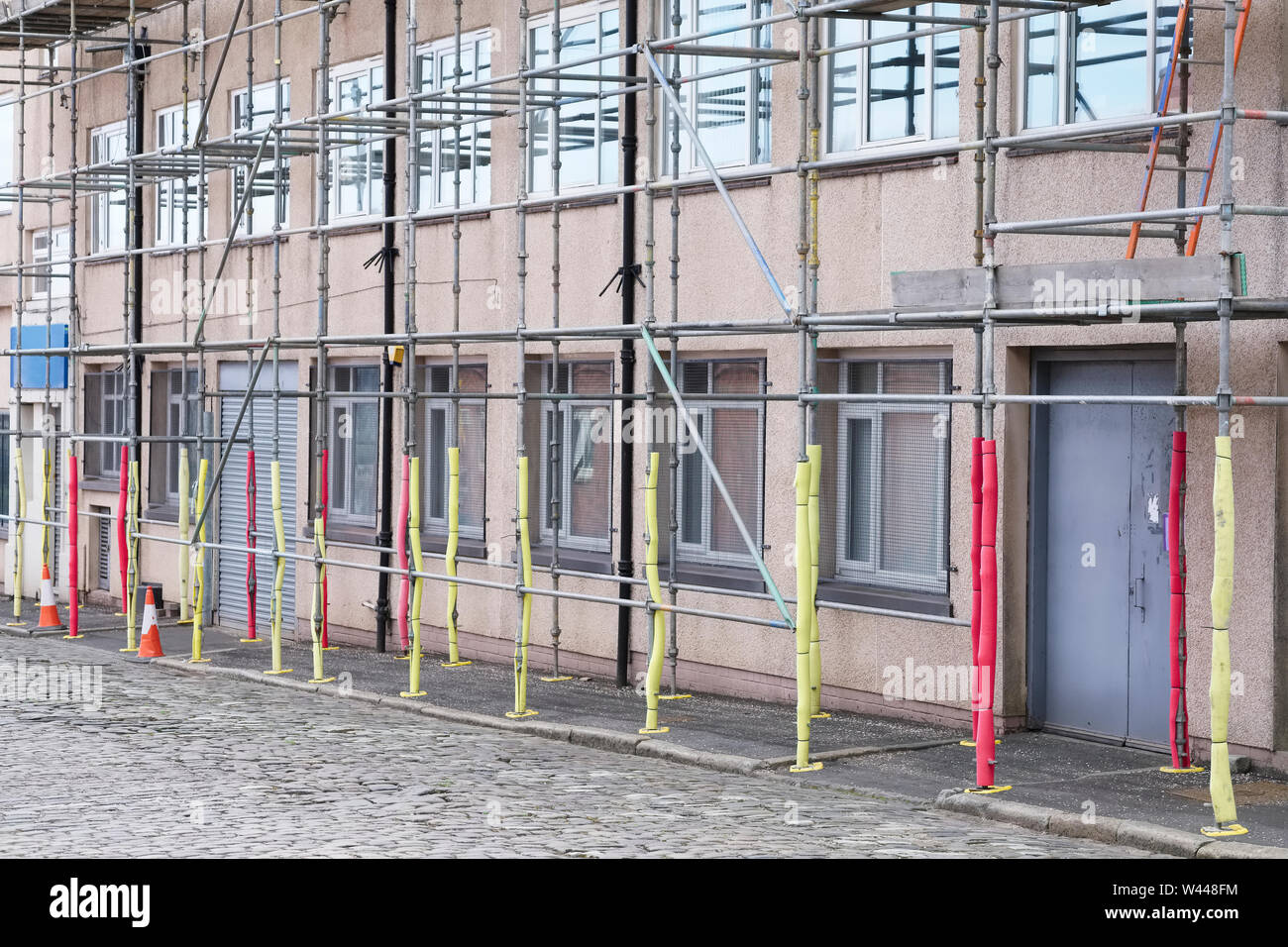 Scaffold pole and platforms erected on cobbled street with red and ...