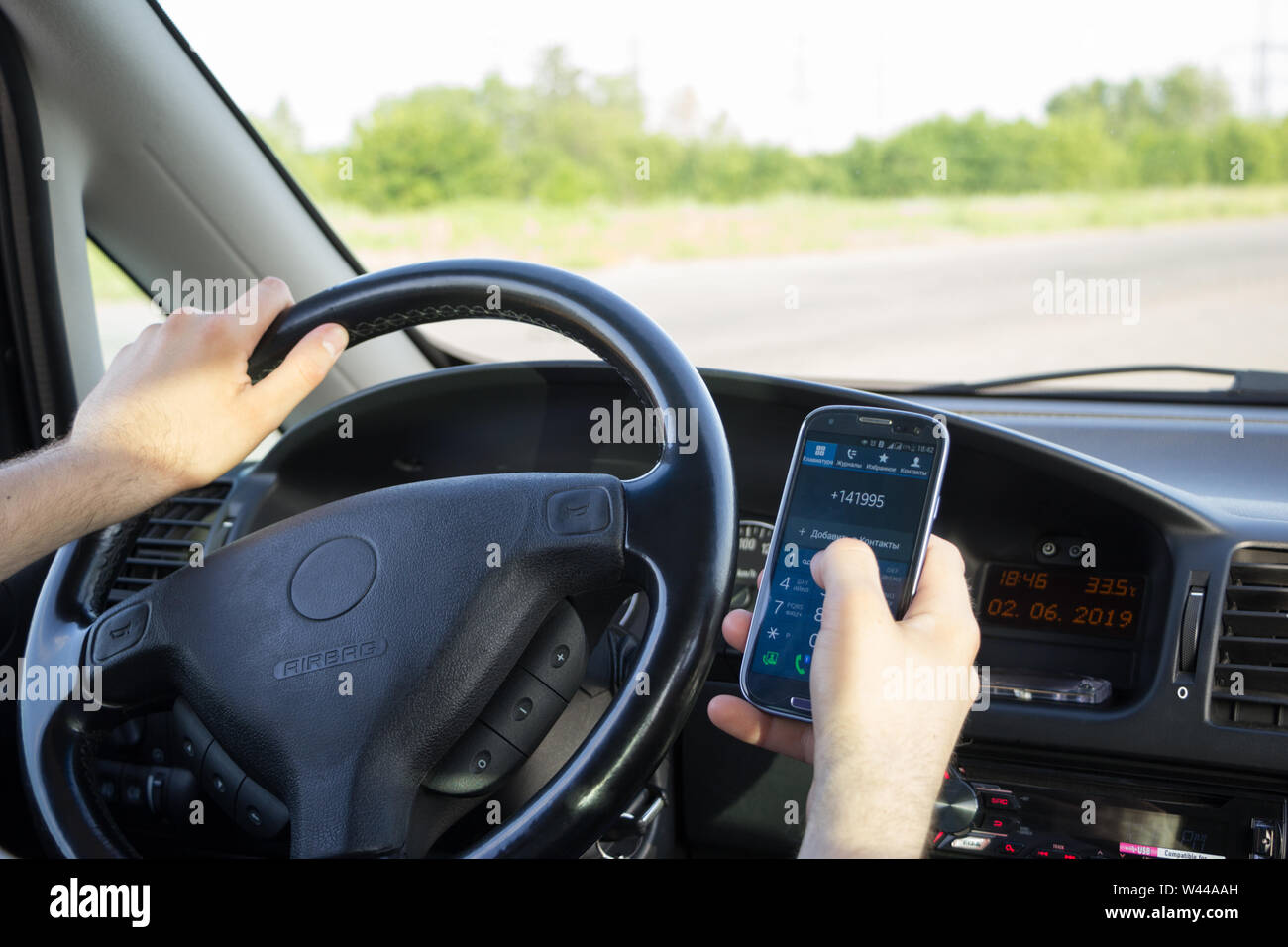 A man dials a phone number on touch screen of smartphone while driving ...
