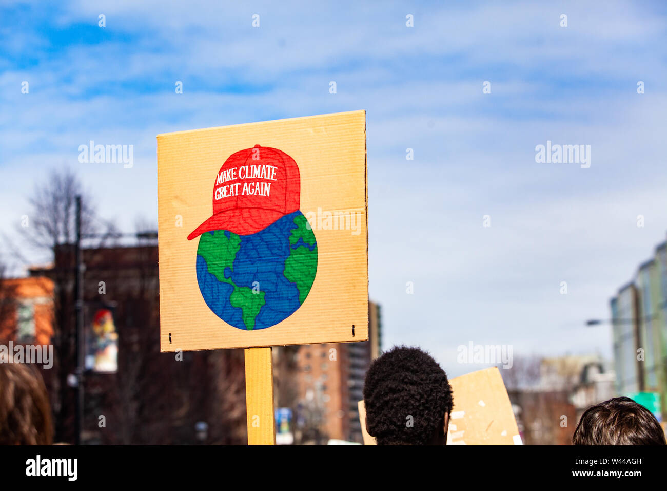 A closeup view of a cardboard sign with a picture of planet earth wearing Trump's cap, saying ...