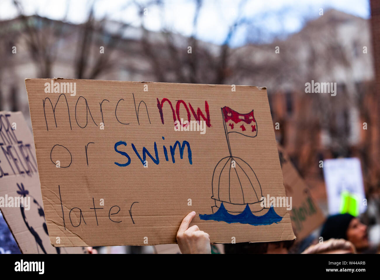 A cardboard sign is viewed close up saying march now or swim later as ...