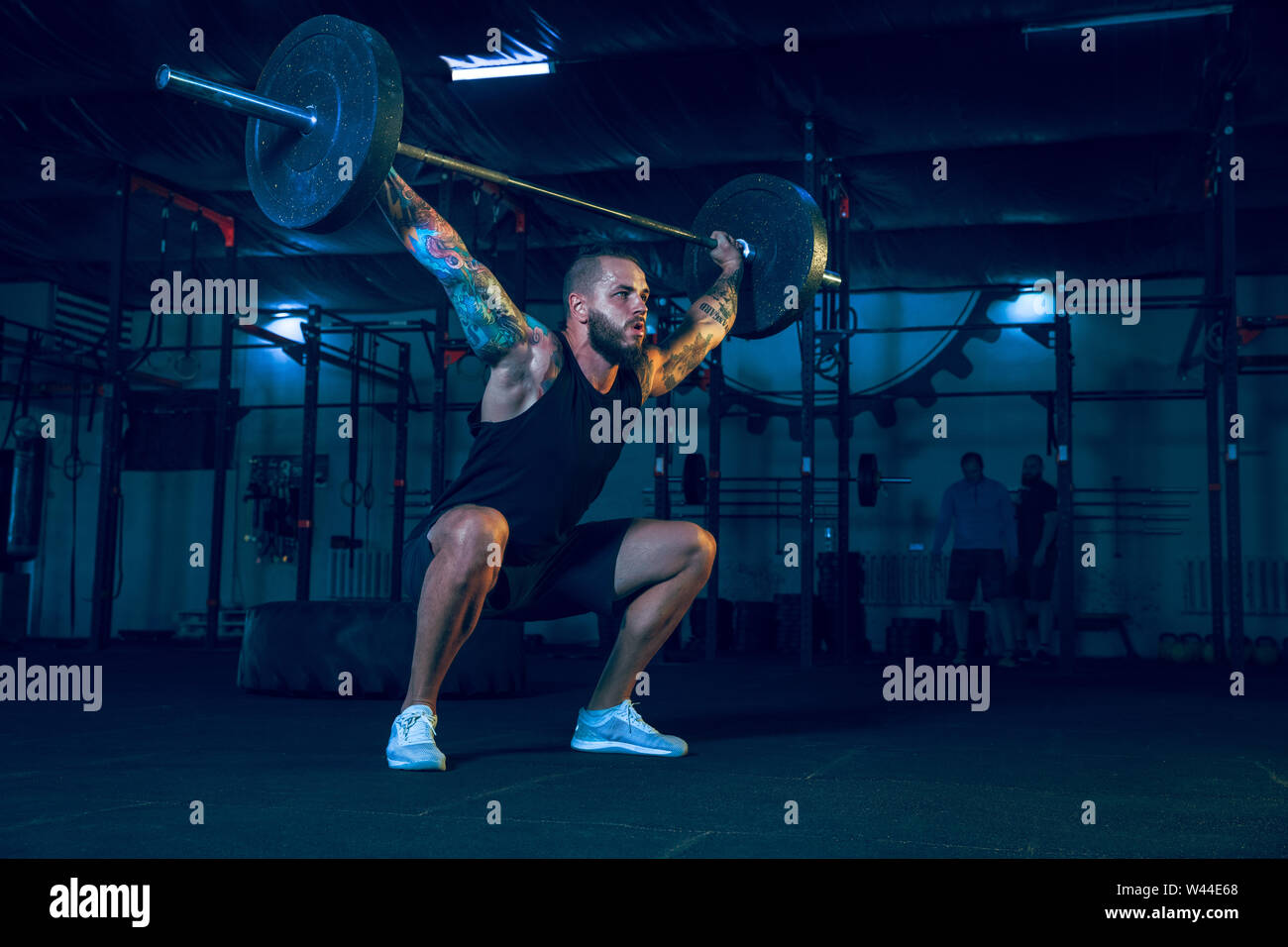 Young healthy man athlete doing exercise with the barbell in the gym ...