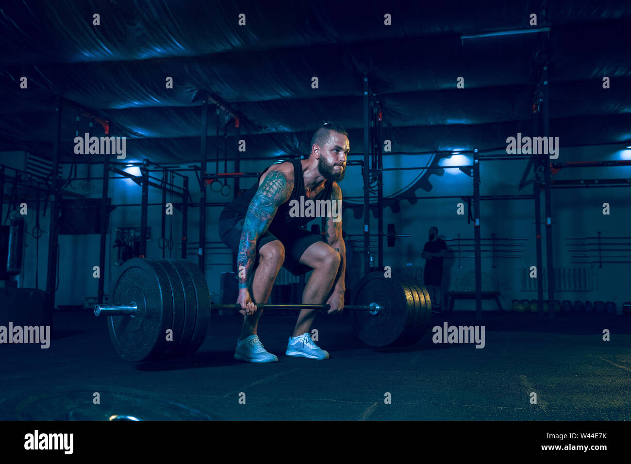 Young healthy man athlete doing exercise with the barbell in the gym ...