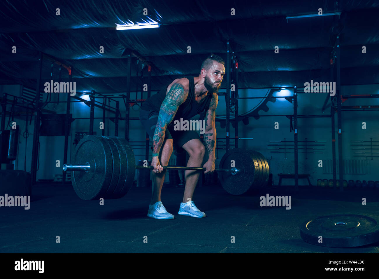 Young healthy man athlete doing exercise with the barbell in the gym ...