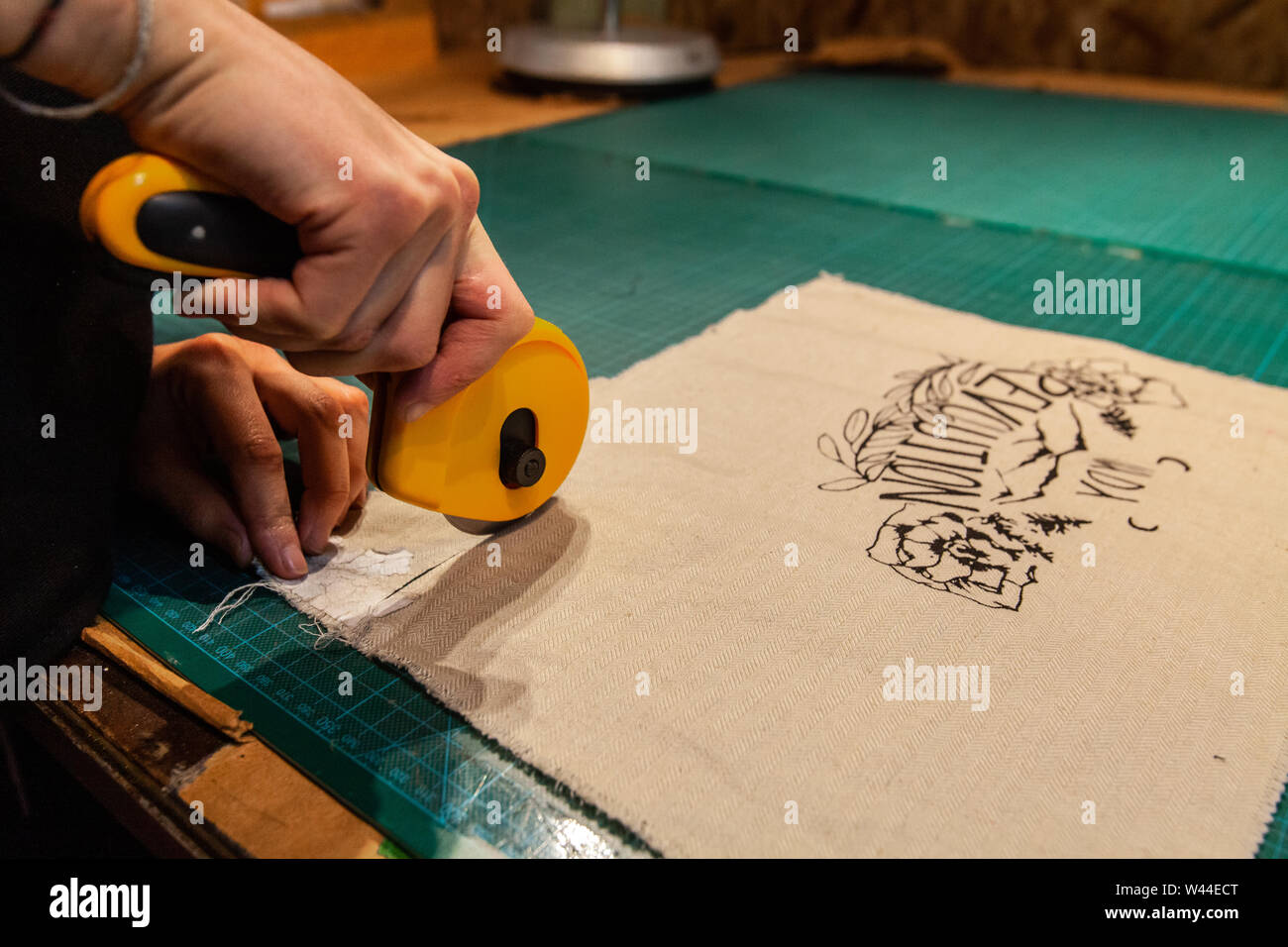 A close-up view on the hands of a quilter using a rotary cutter on a ...