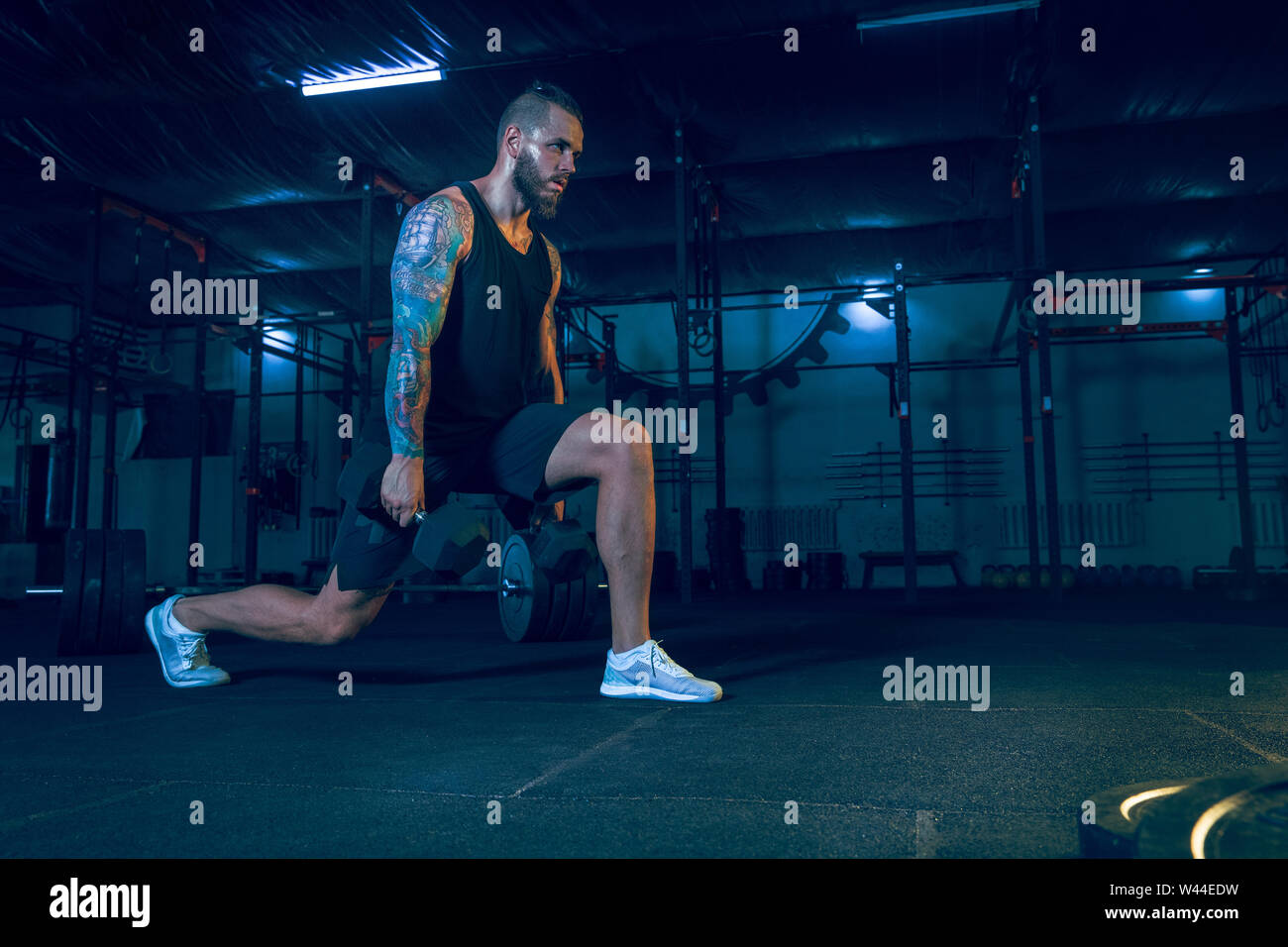 Young healthy man athlete doing exercise with the weights in the gym ...