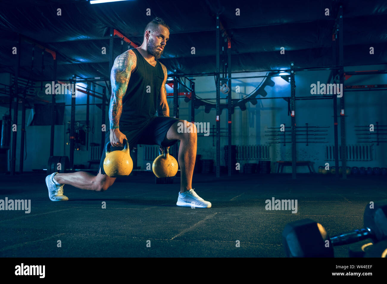 Young healthy man athlete doing exercise with the weights in the gym ...
