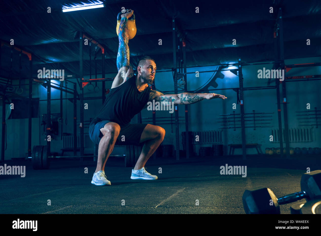 Young healthy man athlete doing exercise with the weights in the gym ...
