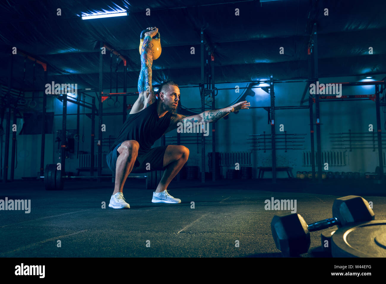 Young healthy man athlete doing exercise with the weights in the gym ...