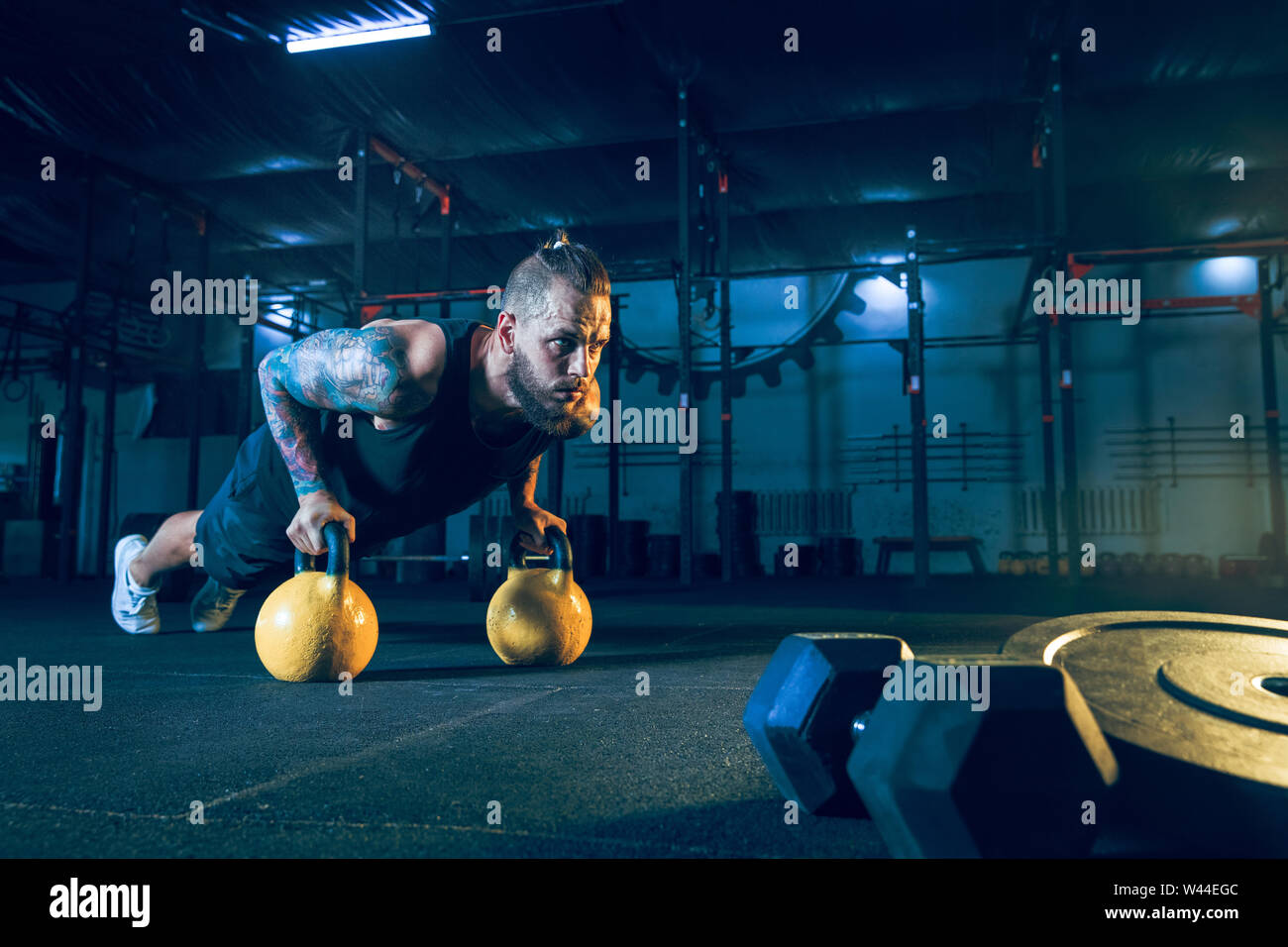 Young healthy man athlete doing push-ups with the weights in the gym ...