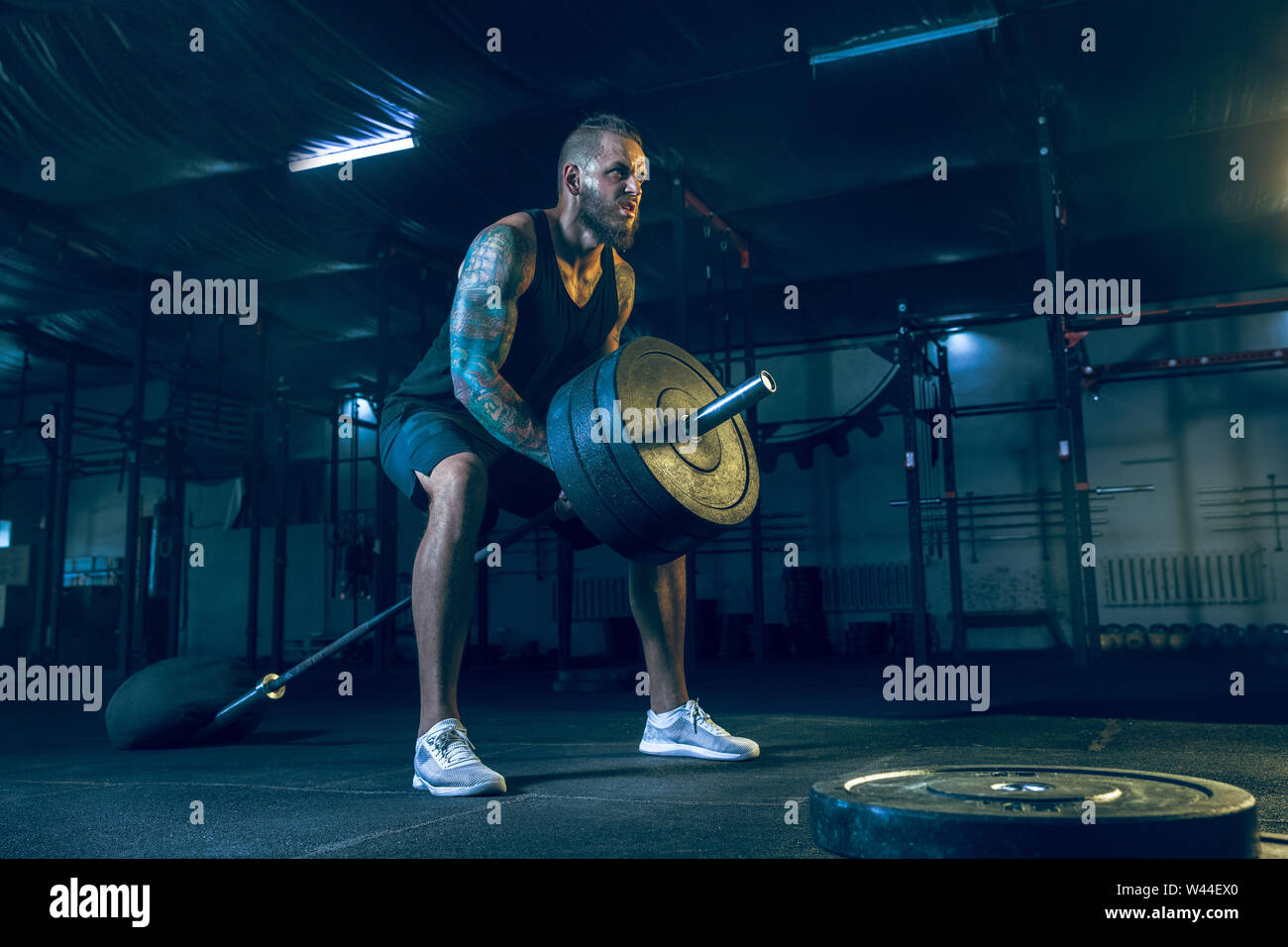 Young healthy man athlete doing exercise with the barbell in the gym ...