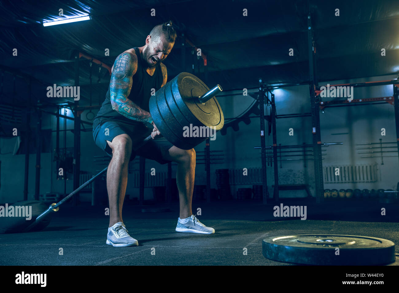 Young healthy man athlete doing exercise with the barbell in the gym ...
