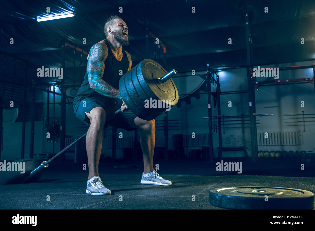 Young healthy man athlete doing exercise with the barbell in the gym ...