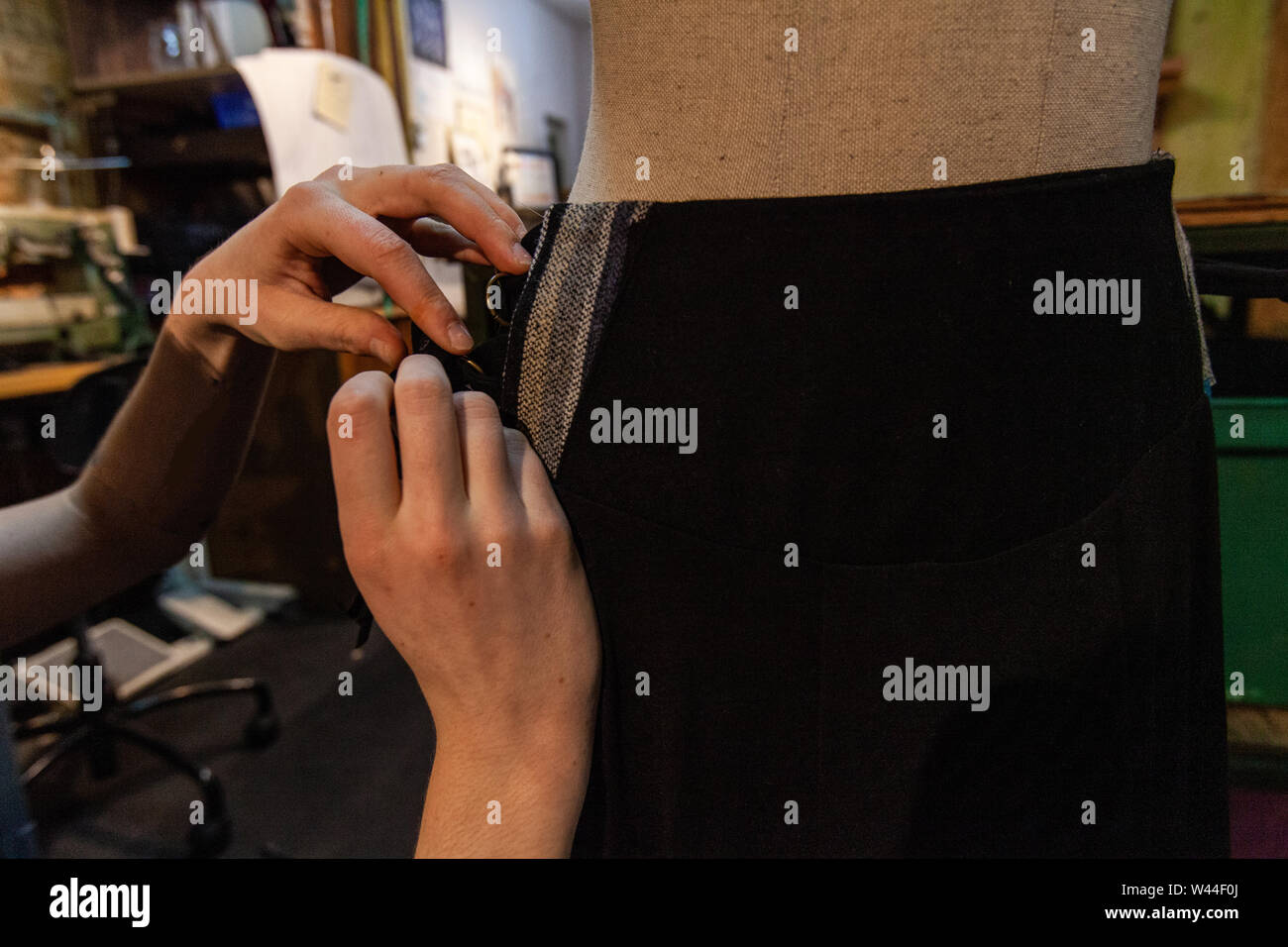 A close-up view on the hands of a tailor fitting a new black dress to a ...