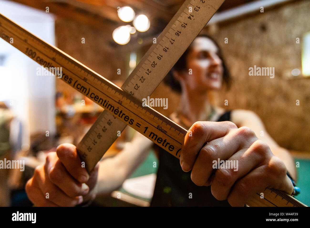 A female fashion worker stands inside an atelier, she holds two metric ...
