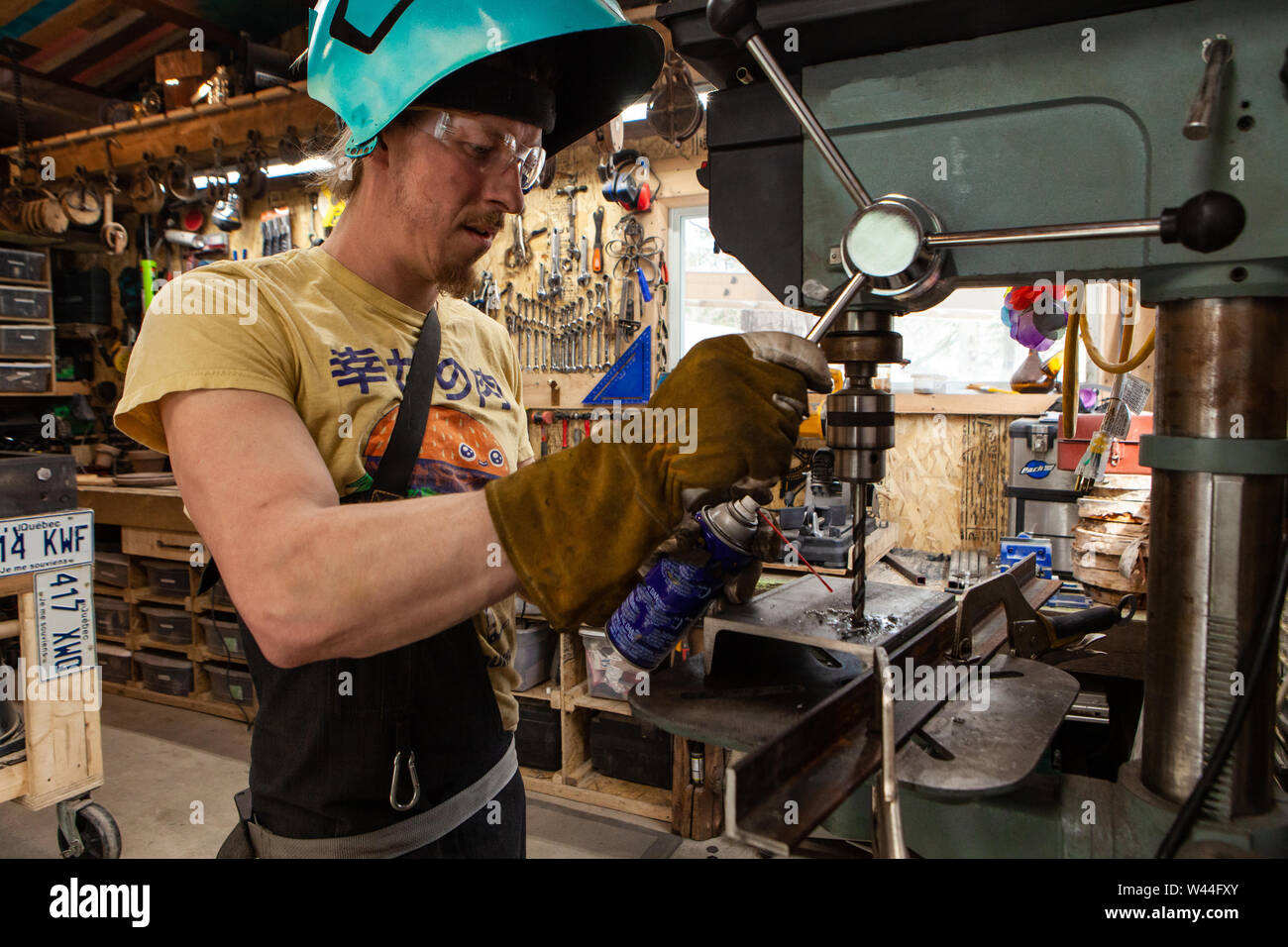 A Caucasian male operates drill press inside his workshop to bore a ...