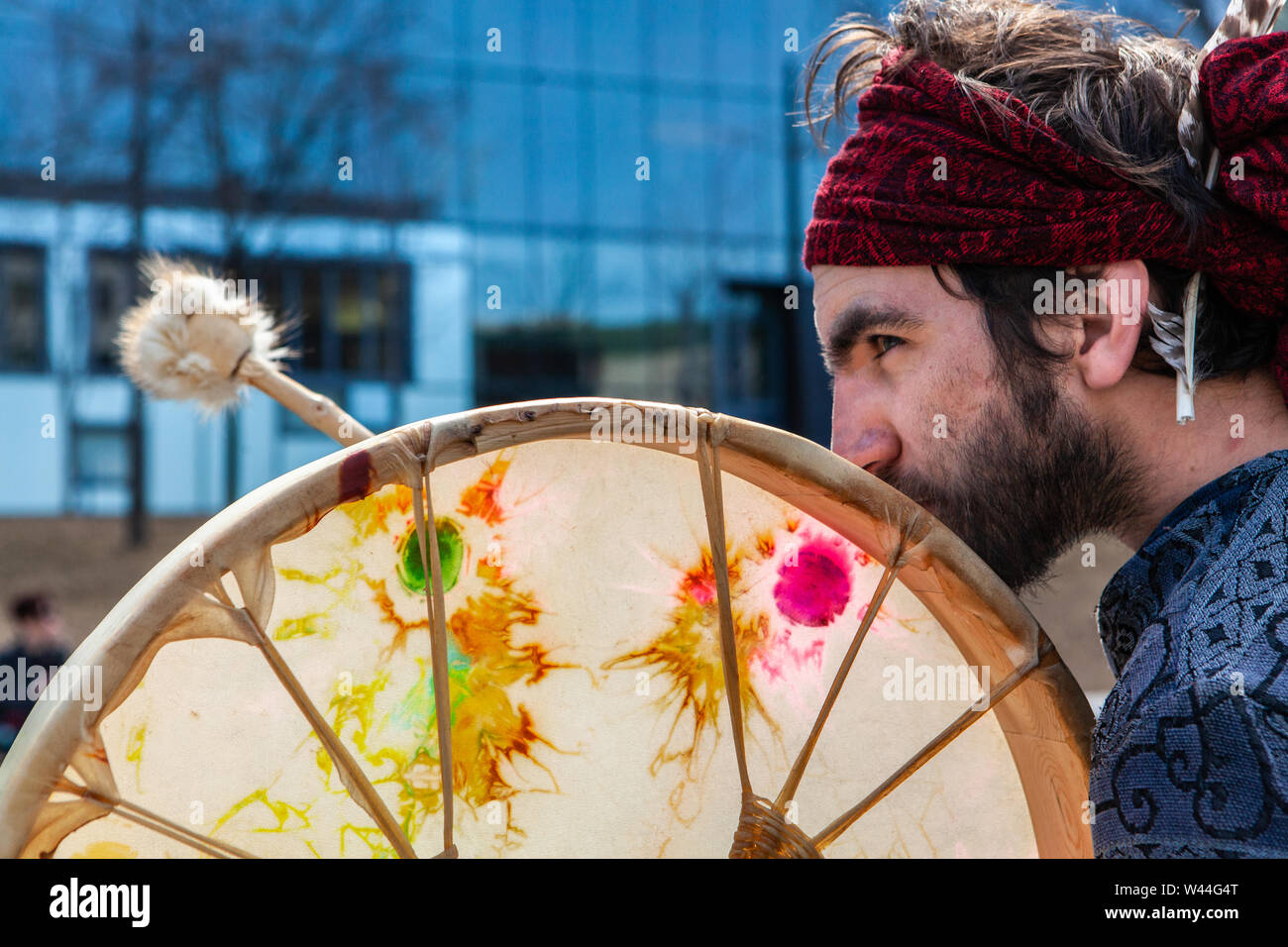 A male pagan is viewed from the side, holding a traditional drum to his ...
