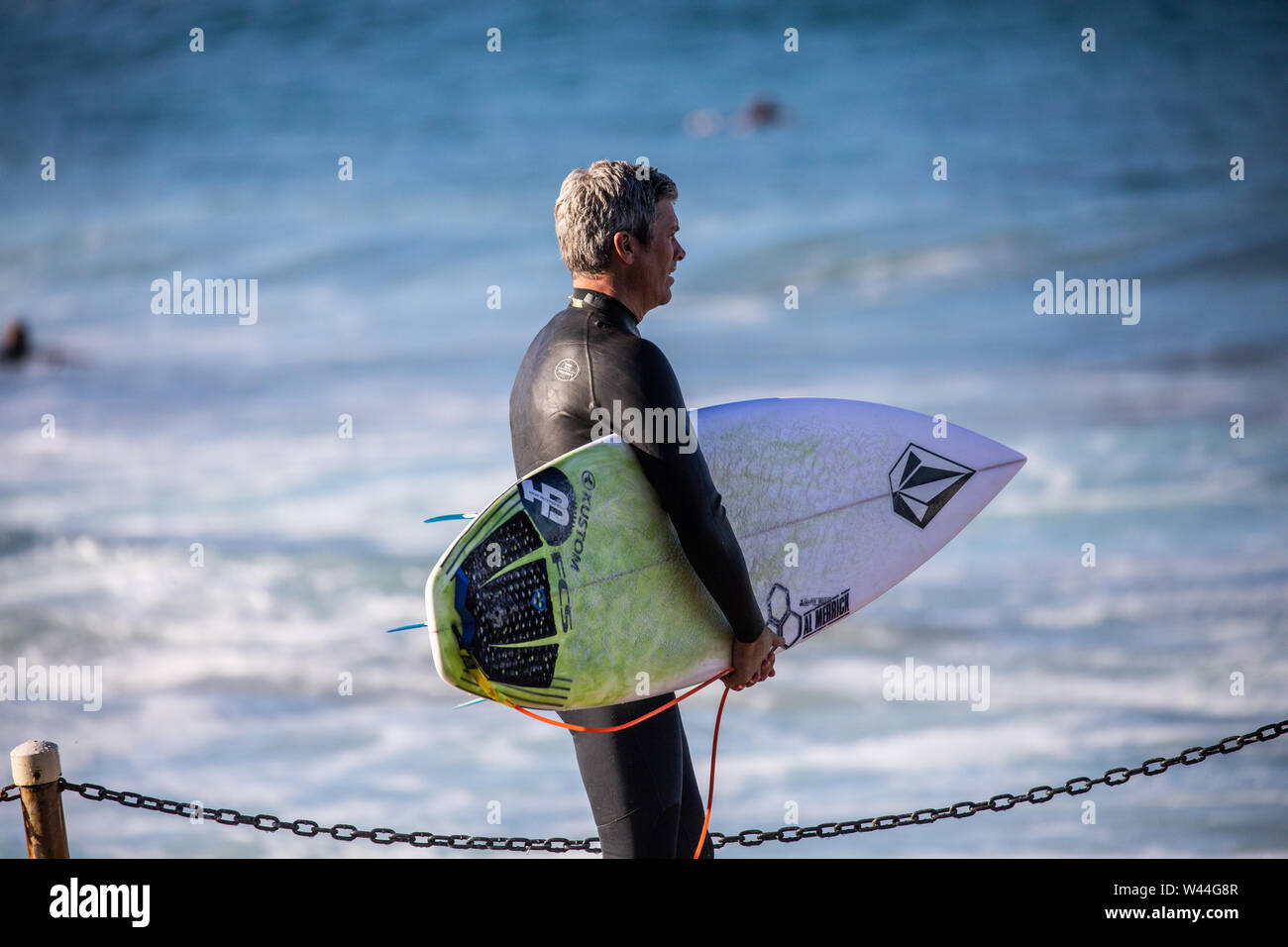 Australian man carries his surfboard to the ocean for a surf on the ...
