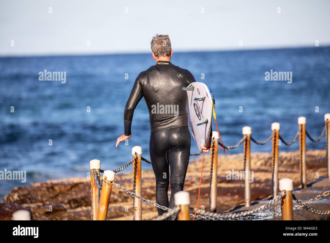 Australian man carries his surfboard to the ocean for a surf on the ...