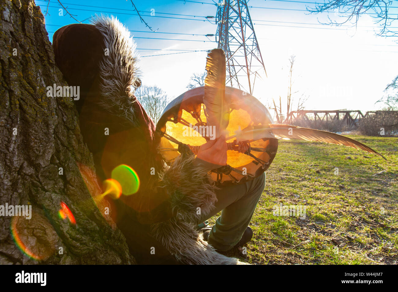 A shaman is viewed from behind as he sits beneath a tree in a nature ...