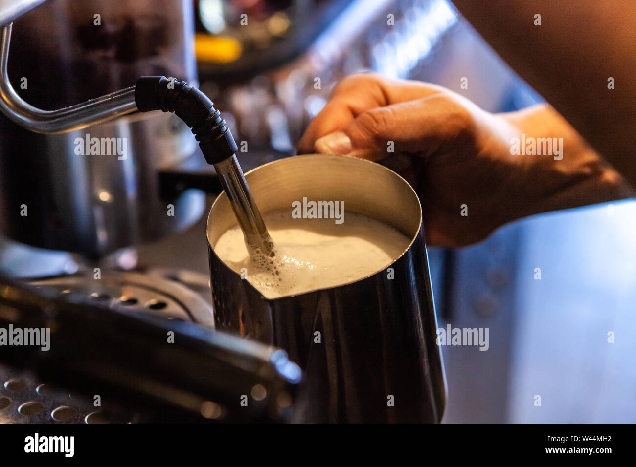 A closeup view on a person holding a jug of milk under the steam baffle ...