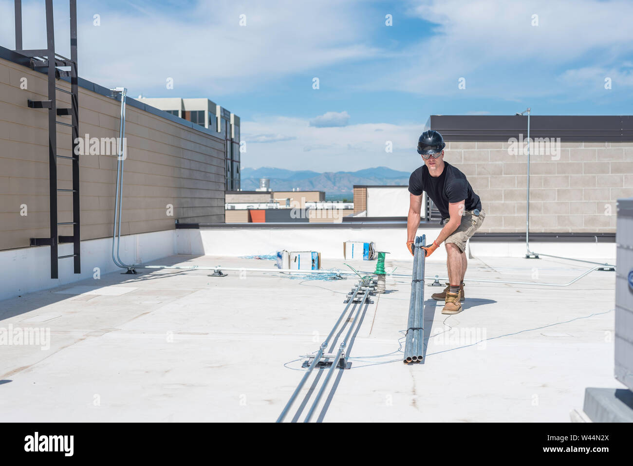 Electrician lifting up a bundle of conduit on a roof top Stock Photo ...