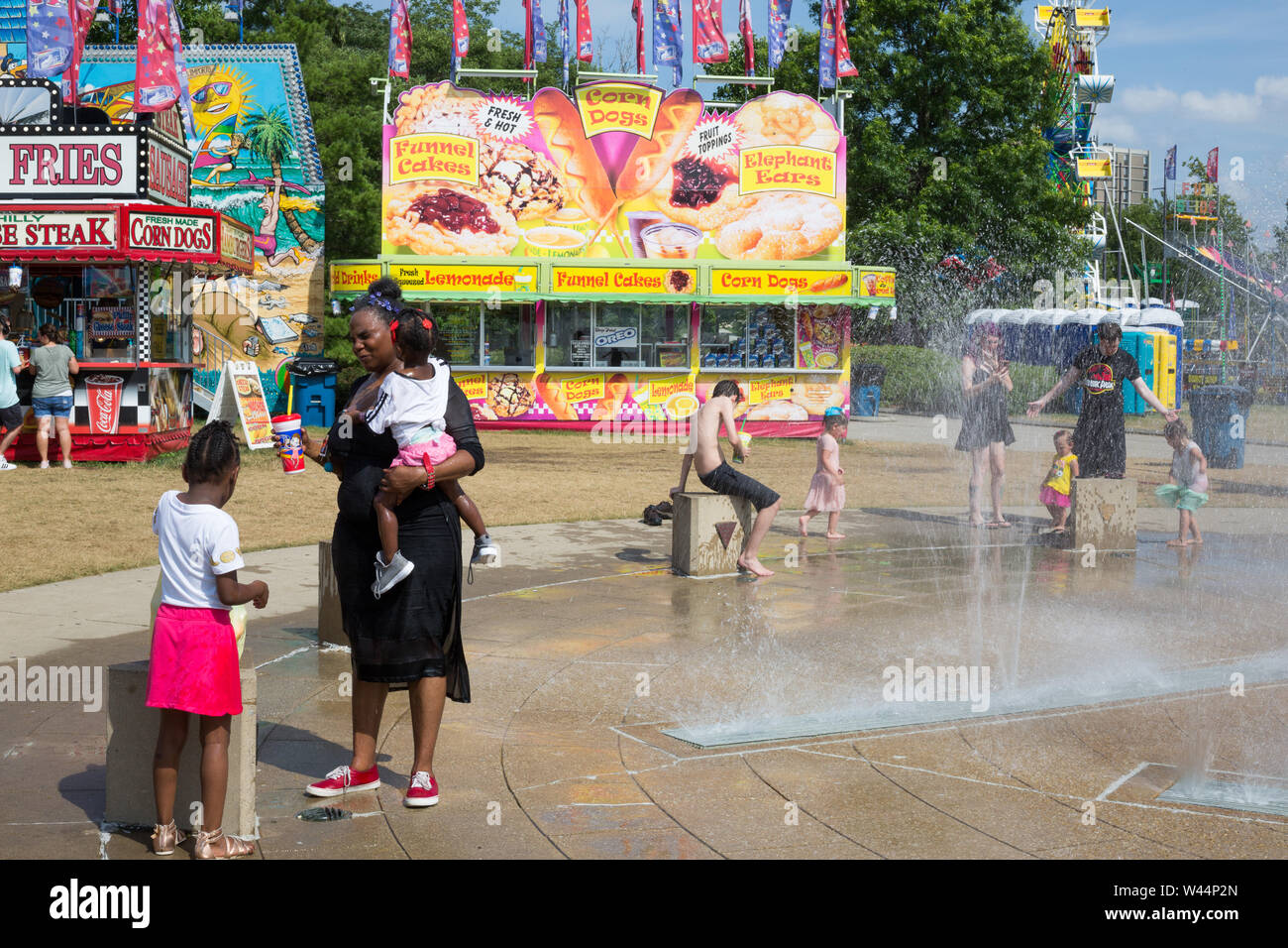 A mother encourages her timid daughter to enjoy the splash pad at the ...