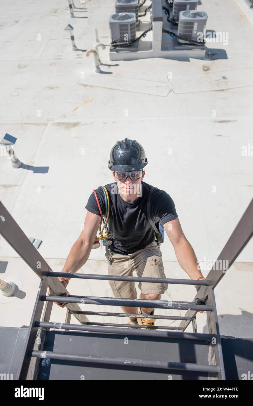 Hvac tech wearing safety gear, climbing down a ladder on a roof top ...