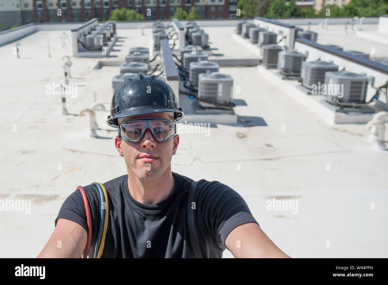 Hvac tech on a roof ladder, with condensing units in the background ...