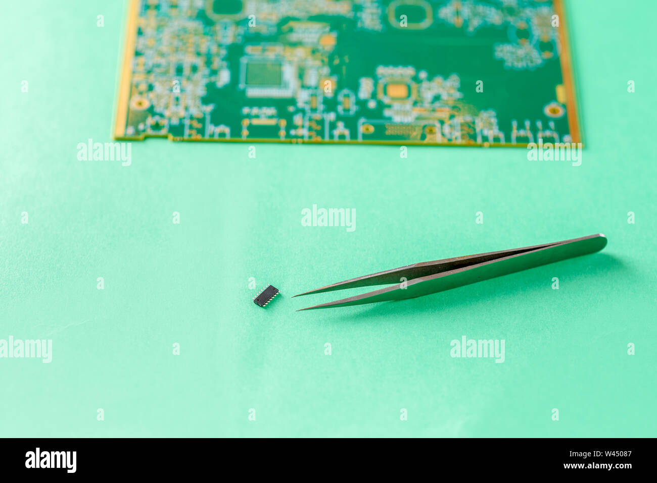 Tweezers, Computer chip and blurred small PCB-printed circuit board on ...