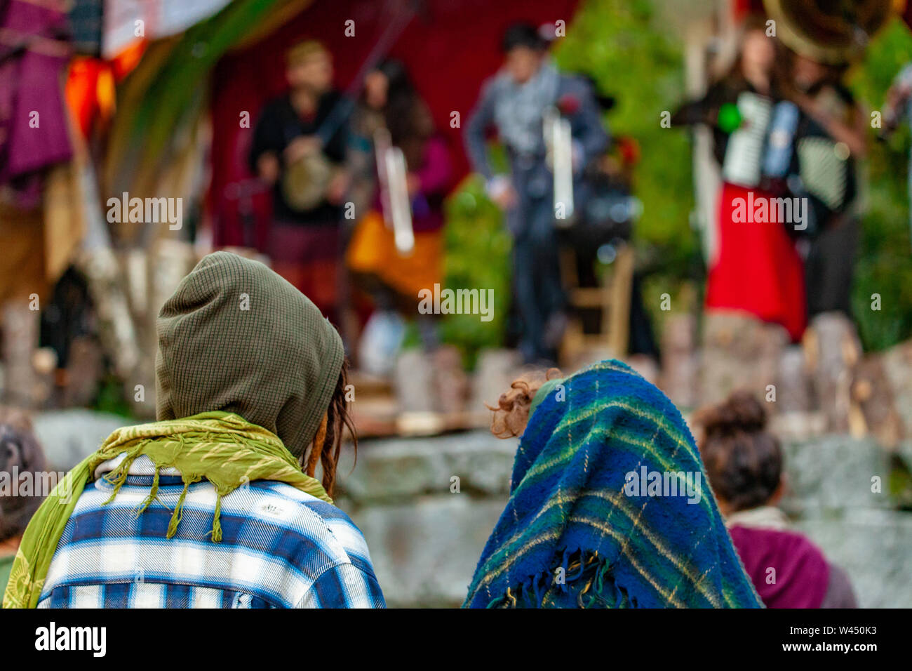 Hippies are viewed from behind, watching a blurry band perform folk ...