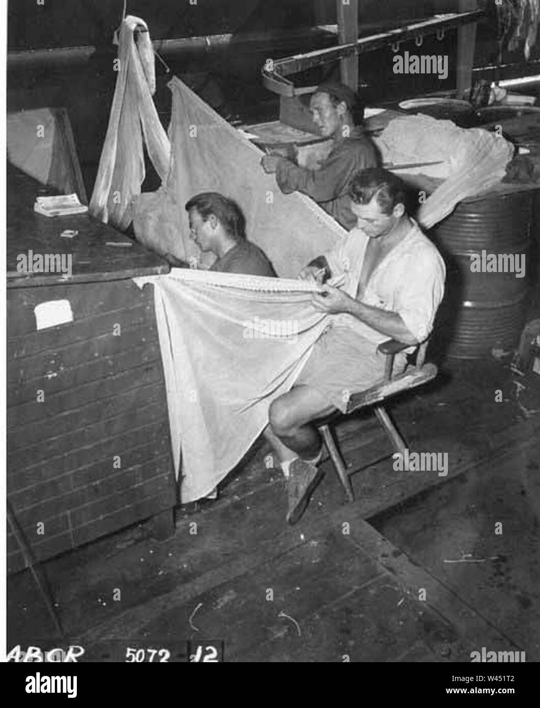Commercial fishermen aboard LSM 382 sewing bait seine on fish nets ...