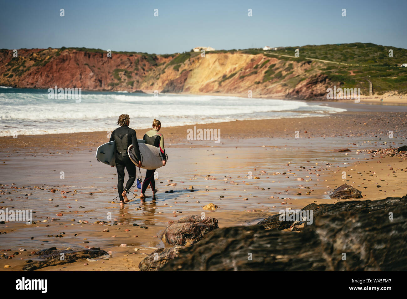 Two surfers carrying their boards along a beach Stock Photo - Alamy