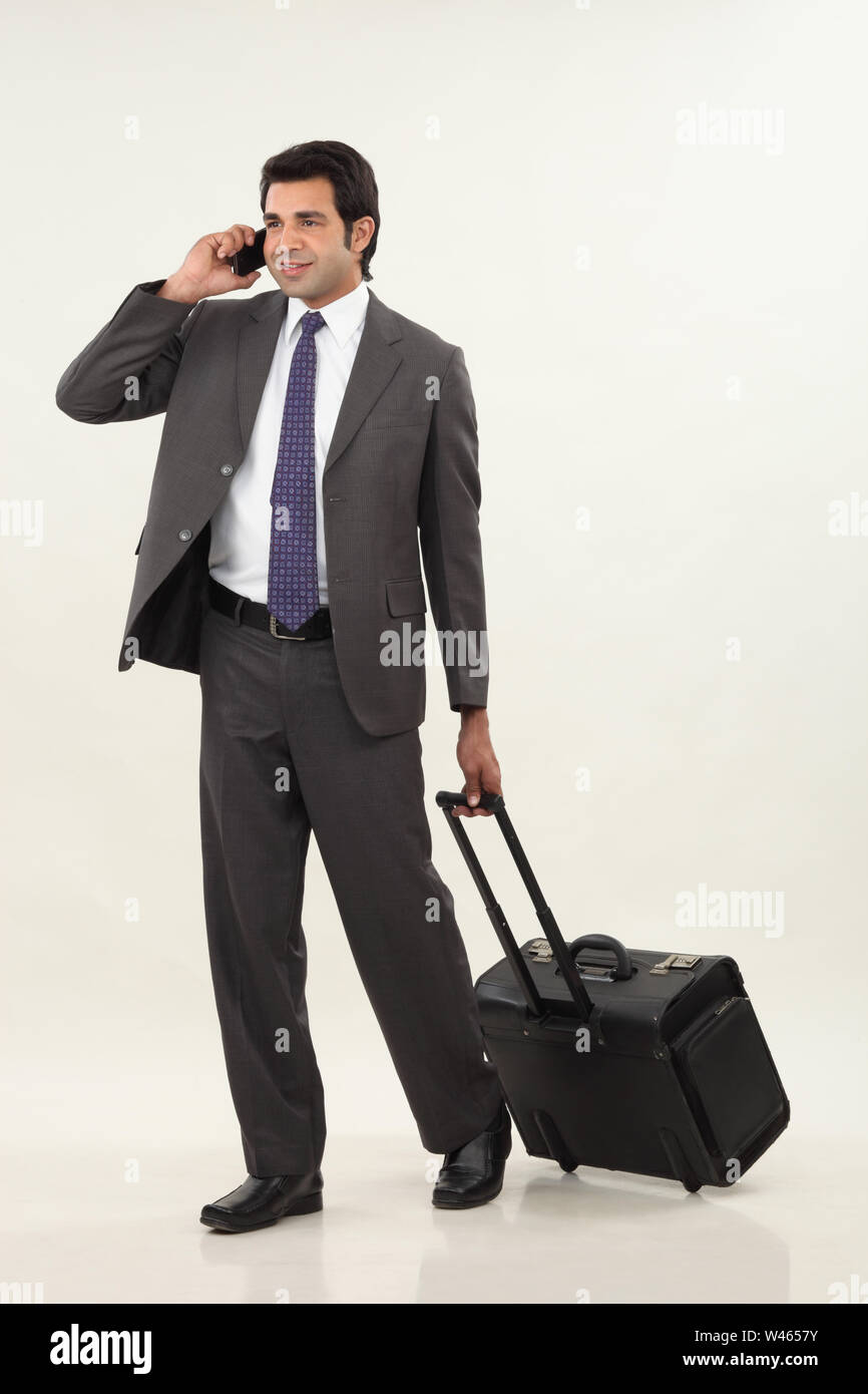 Businessman talking on mobile phone and pulling suitcase Stock Photo ...
