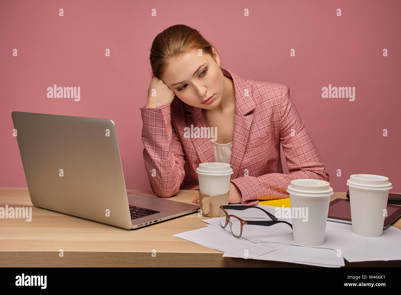 Young woman sits at the table and looks tired, pink background Stock ...