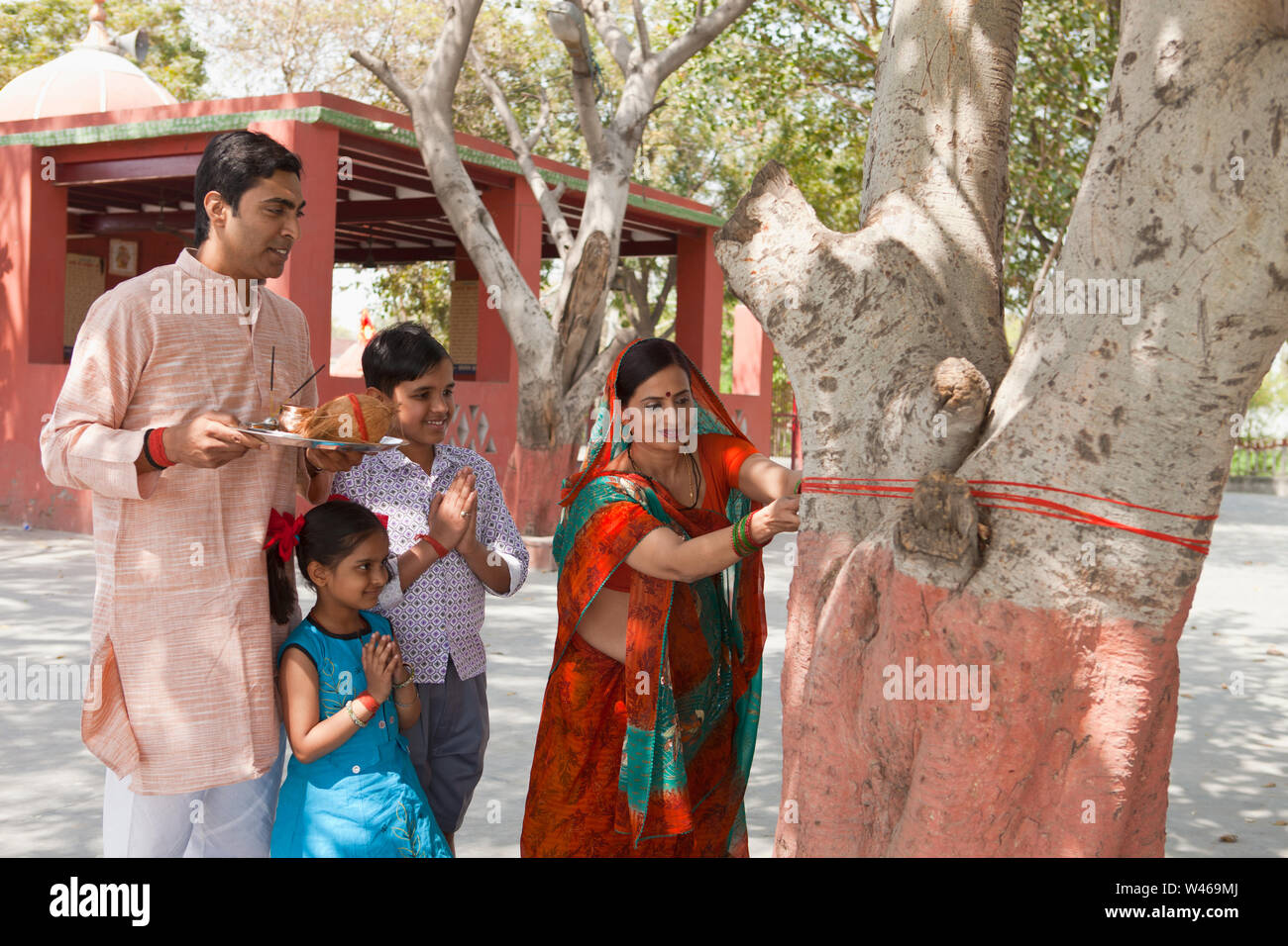 Woman tying thread around a sacred tree with her family Stock Photo - Alamy