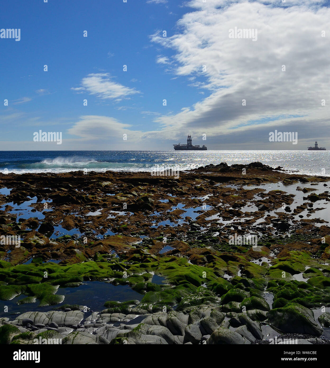 Colorful rocky coast at low tide with oil rigs in the bay and blue sky ...
