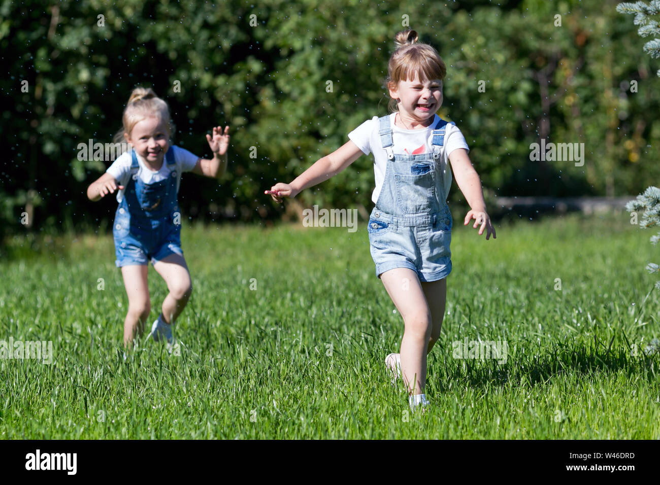 Girls running around the lawn with grass playing with splashes of water ...