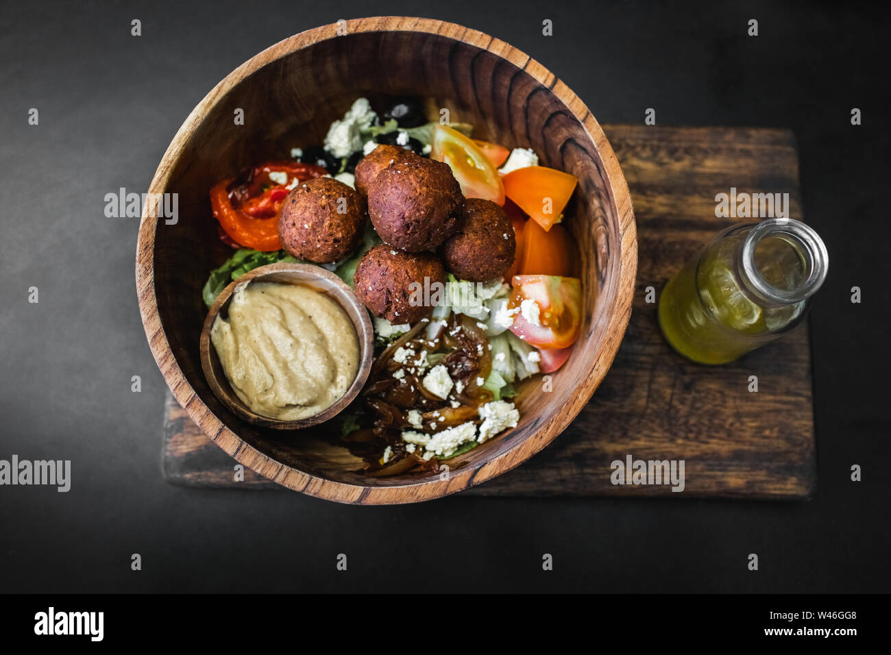 Wooden bowl with falafel balls, hummus and fresh salad. Olive oil in ...