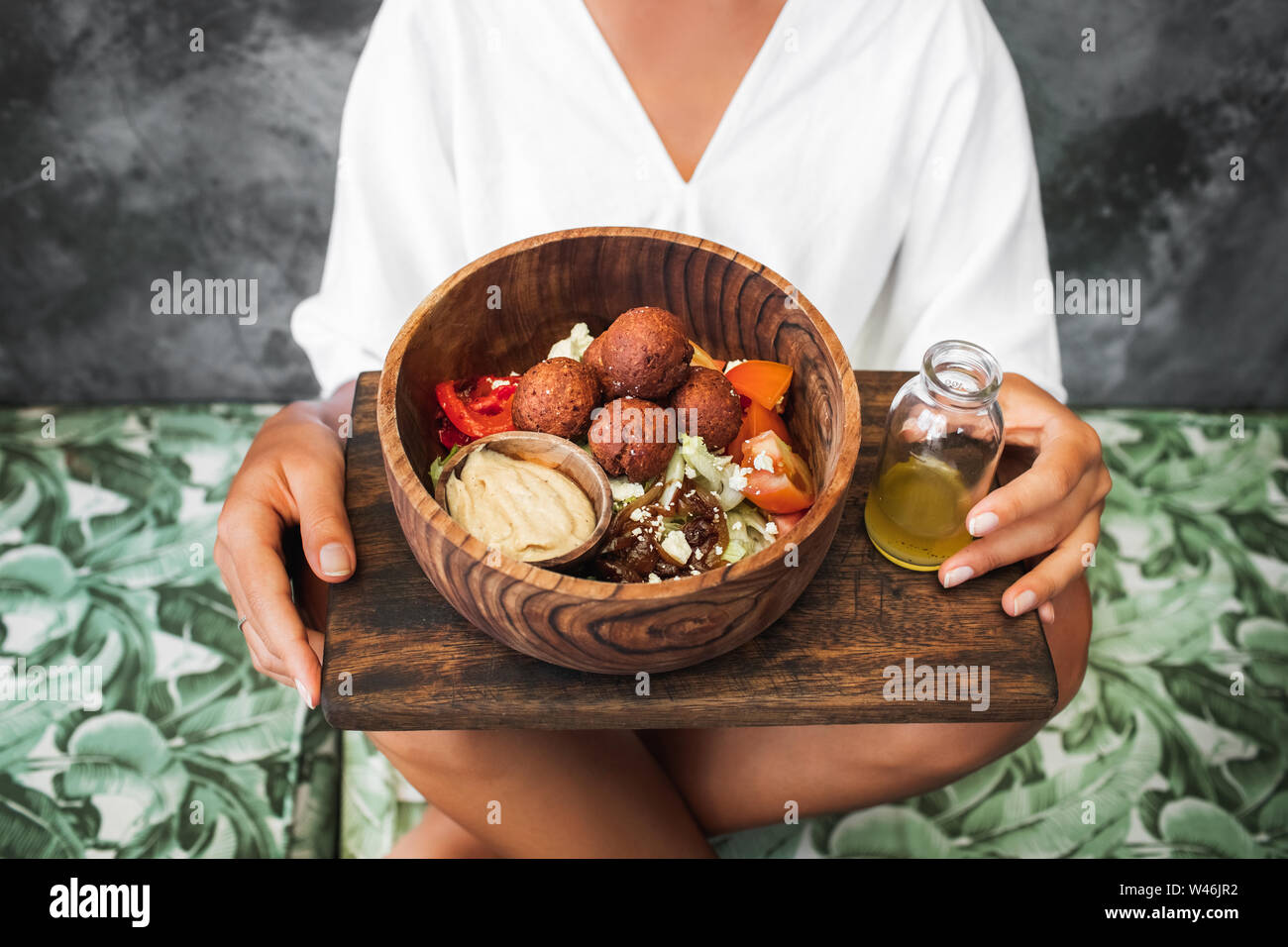 Woman eating falafel balls, hummus and fresh salad in wooden bowl ...