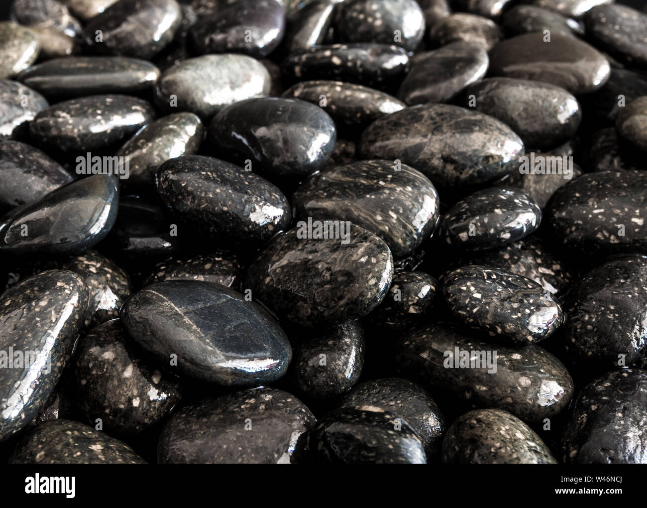 Glossy surface of round black stone on ground beside the waterfall ...