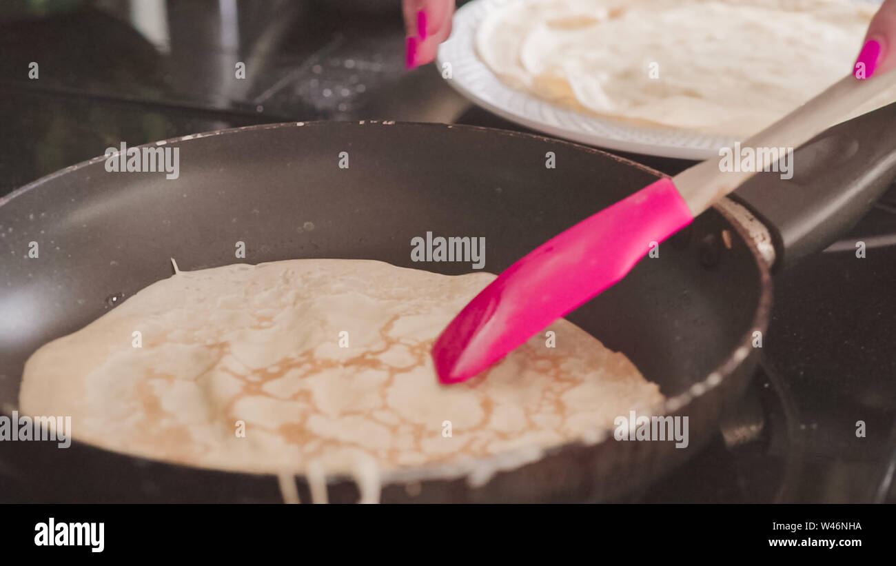 Cooking Russian pancake in old frying pan on top of electric stove ...