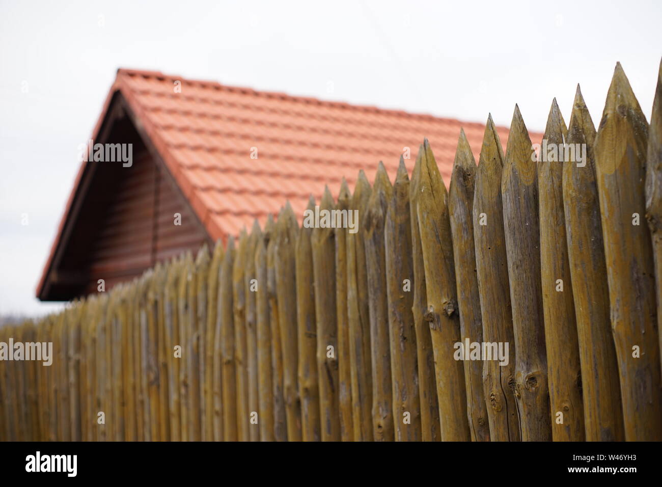 A fence made of sharp wooden stakes against the background of a wooden ...