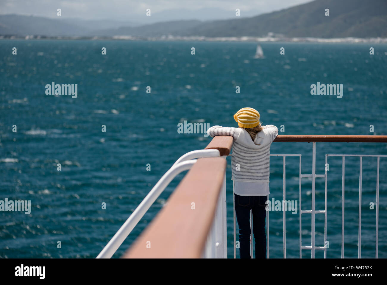 Girl in yellow knit hat looking over railing at the ocean Stock Photo ...
