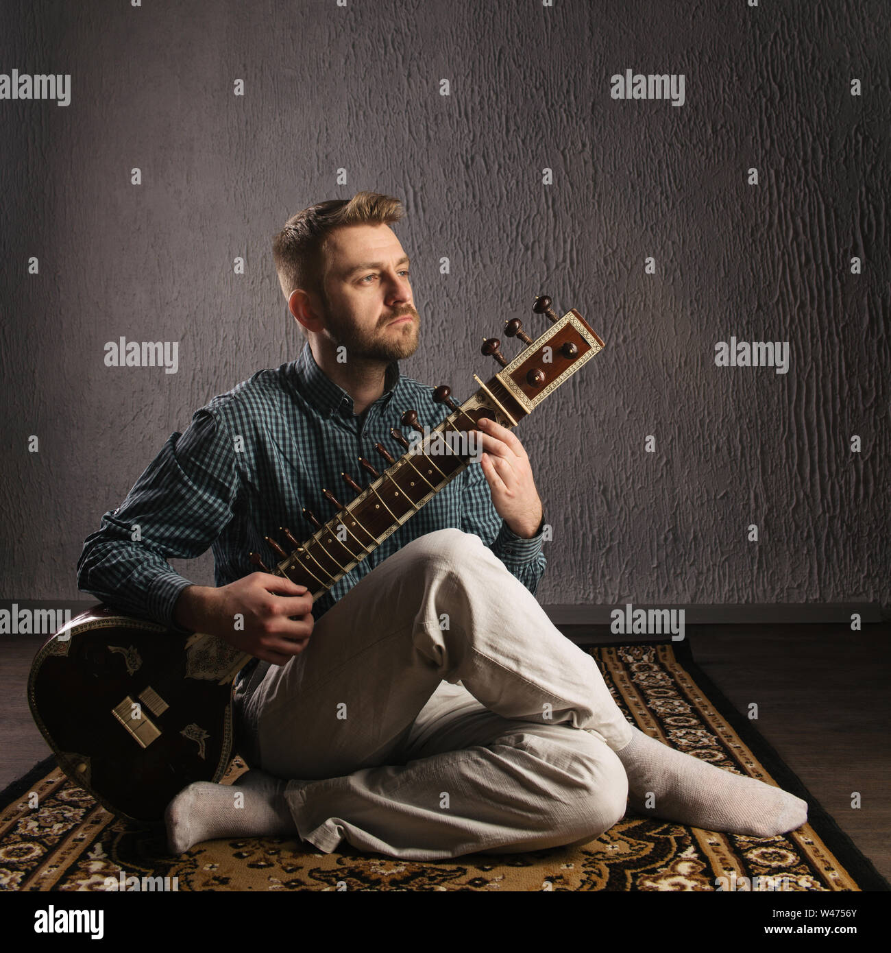 Portrait of a European man playing the sitar sitting on the carpet ...