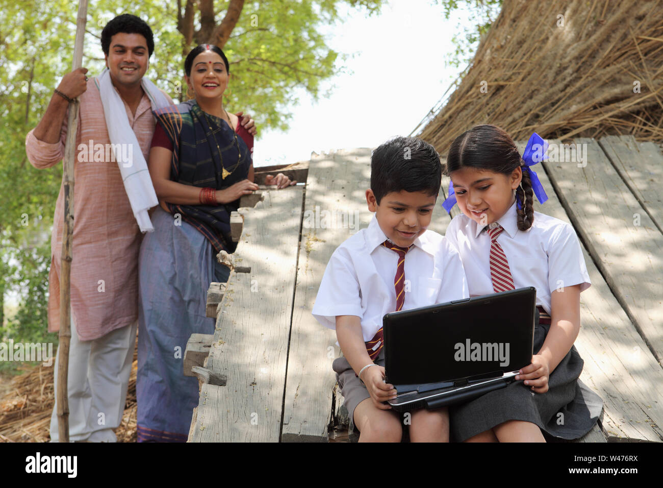 School children using a laptop with their parents looking at them Stock ...