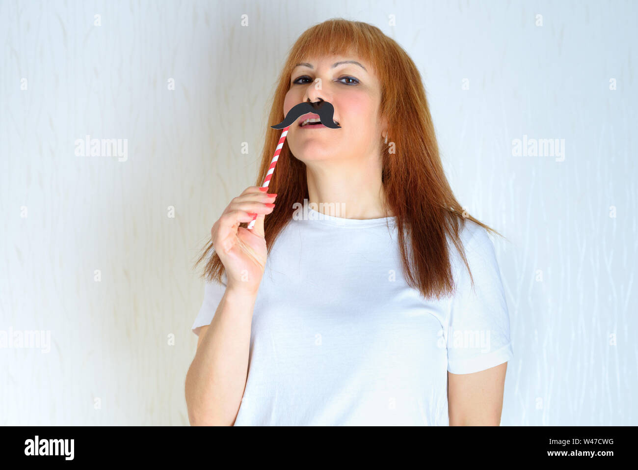 Attractive happy middle aged woman having fun with a fake moustache on ...