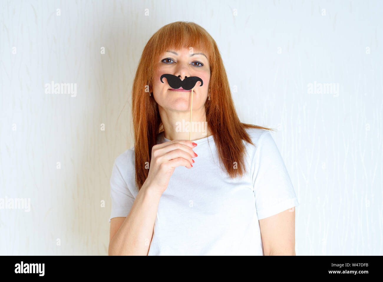 Attractive happy middle aged woman having fun with a fake moustache on ...