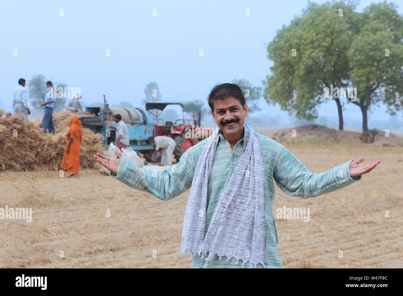 Farmer smiling in a field with farm workers working in the background ...