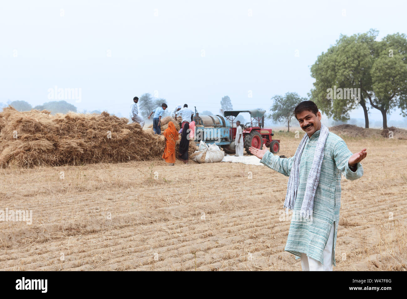 Farmer smiling in a field with farm workers working in the background ...