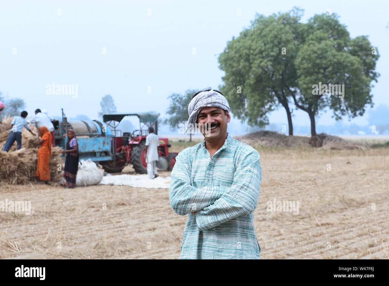 Farmer smiling in a field with farm workers working in the background ...